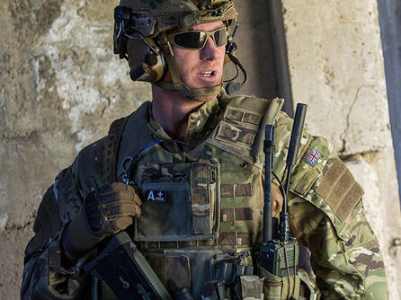 Soldier in front of concrete wall with camouflaged gear and L3Harris ...